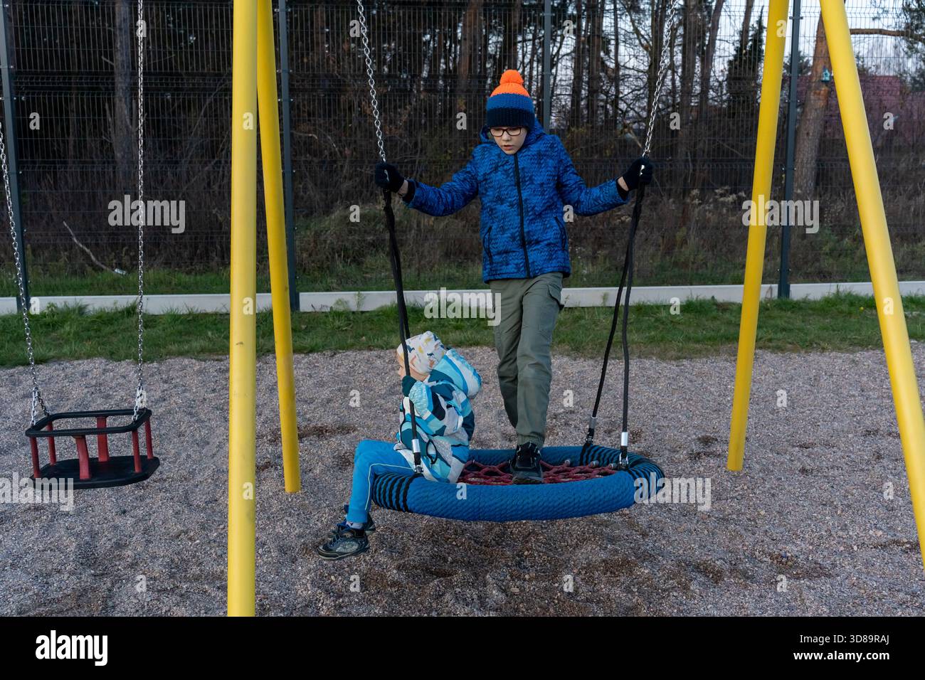 Two brothers playing on nest swing at playground with older boy ...