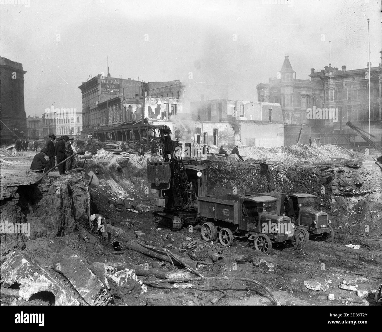 A group of men are standing on a ledge near an excavator and two dump ...