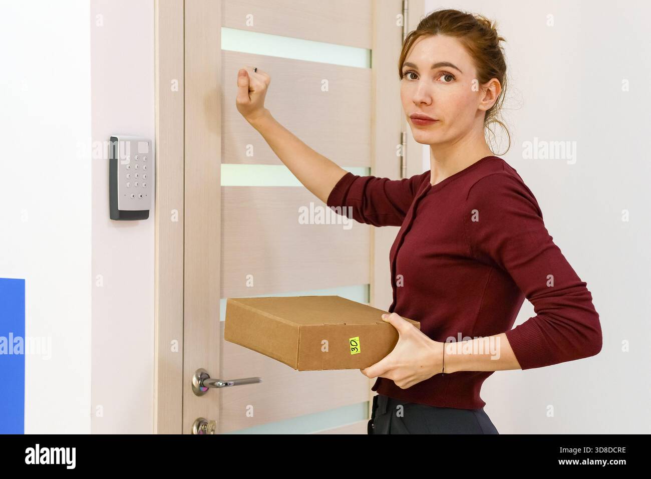 Female courier knocks on wooden door with keypad while carrying labeled ...