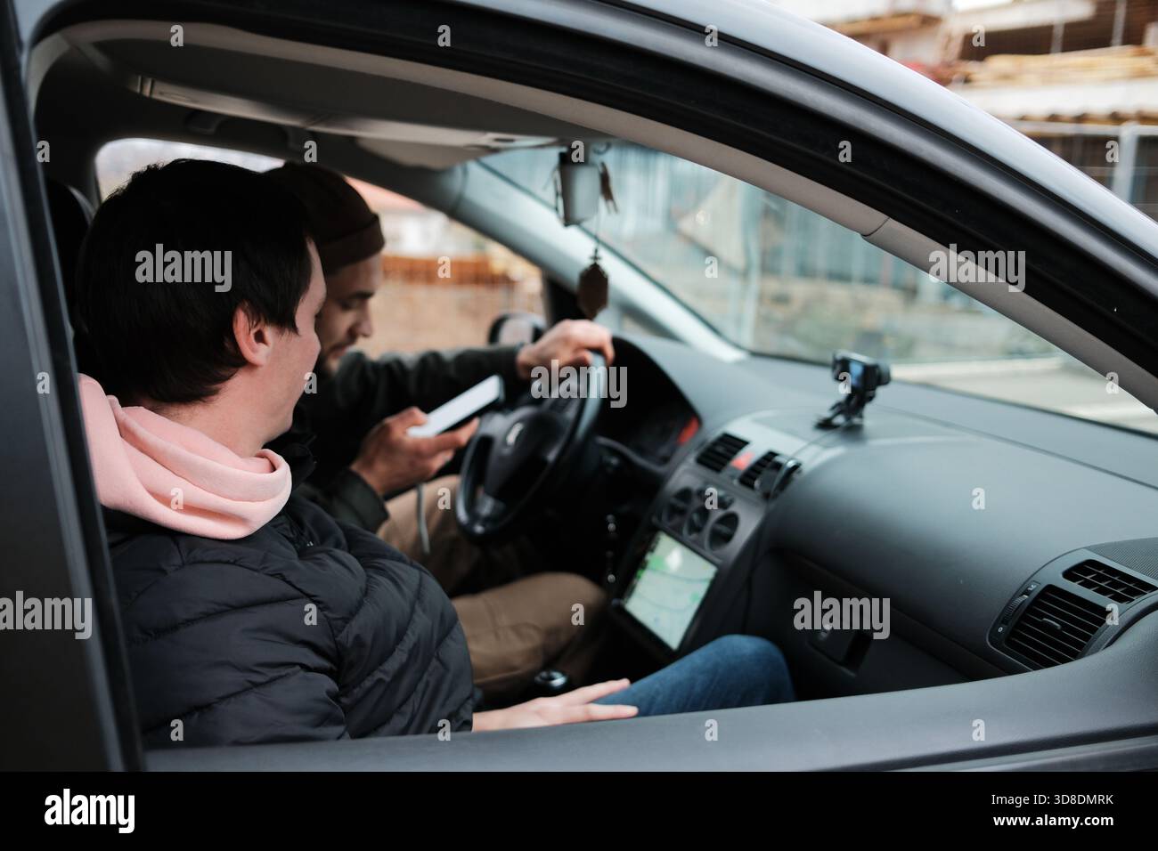Two men sit inside a car while one checks information on a smartphone ...