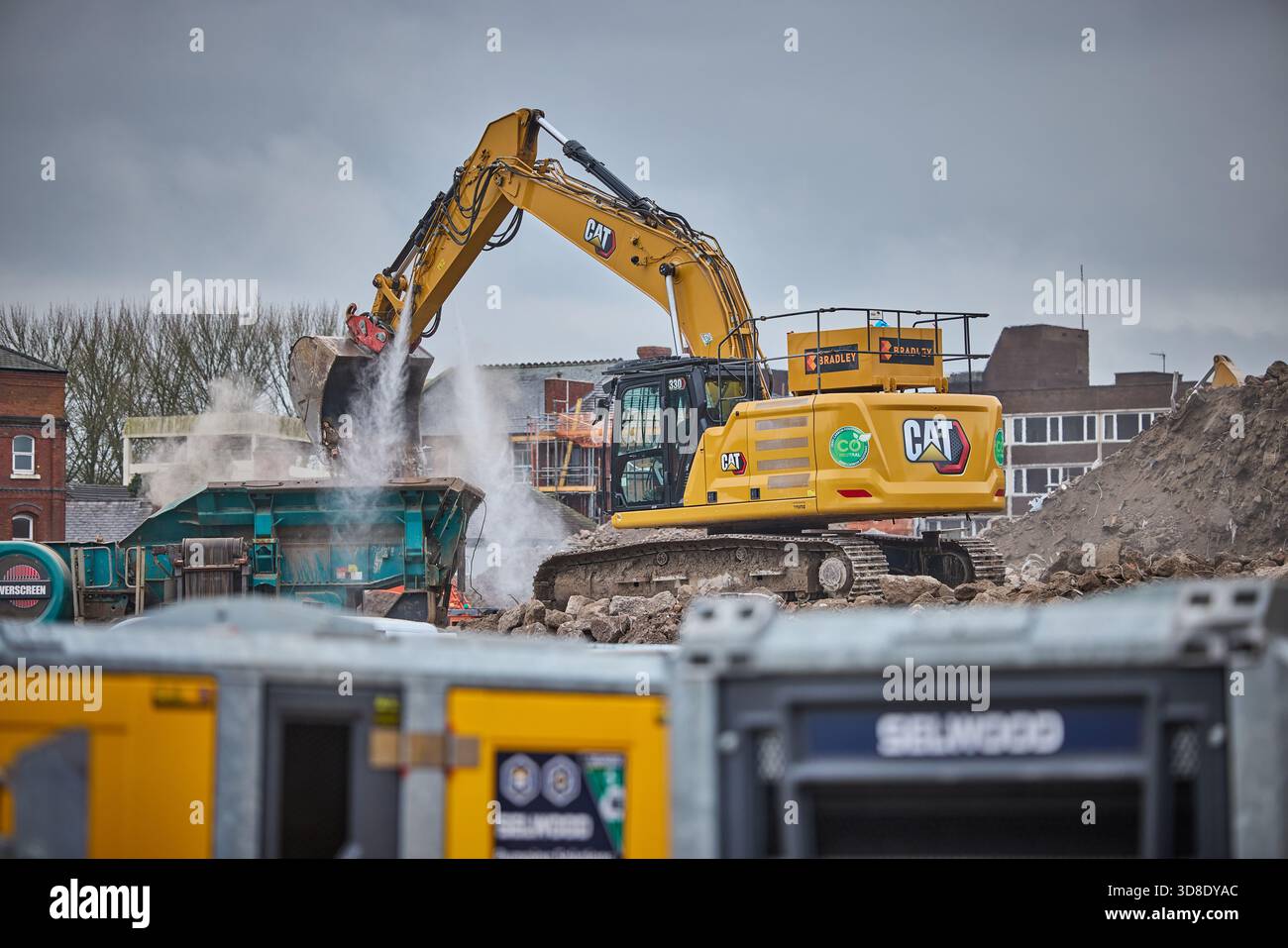 Mechanical digger on tracks working on site with water spray to keep ...