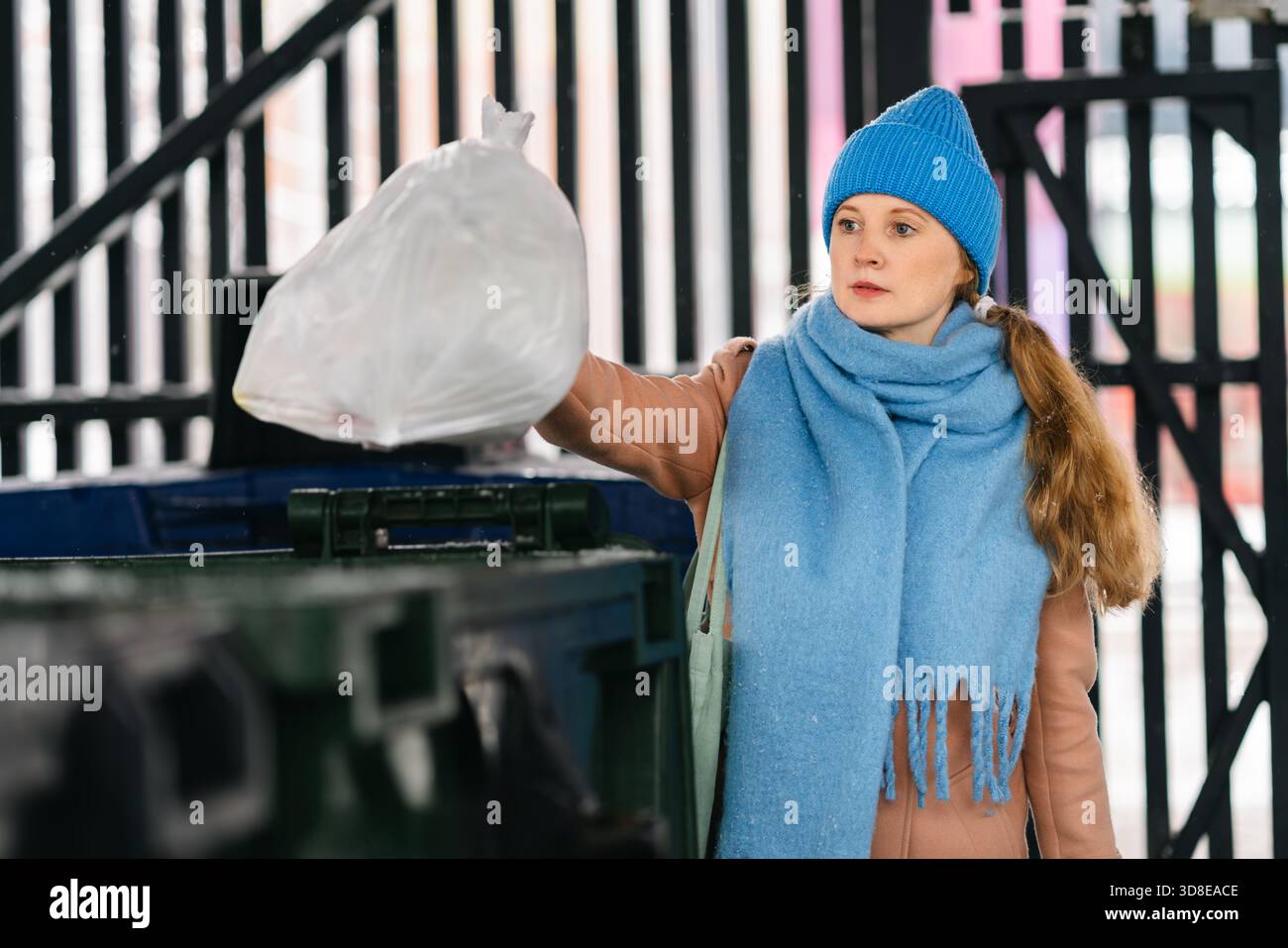 Woman in a coat and hat throws a garbage bag into a trash bin Stock ...