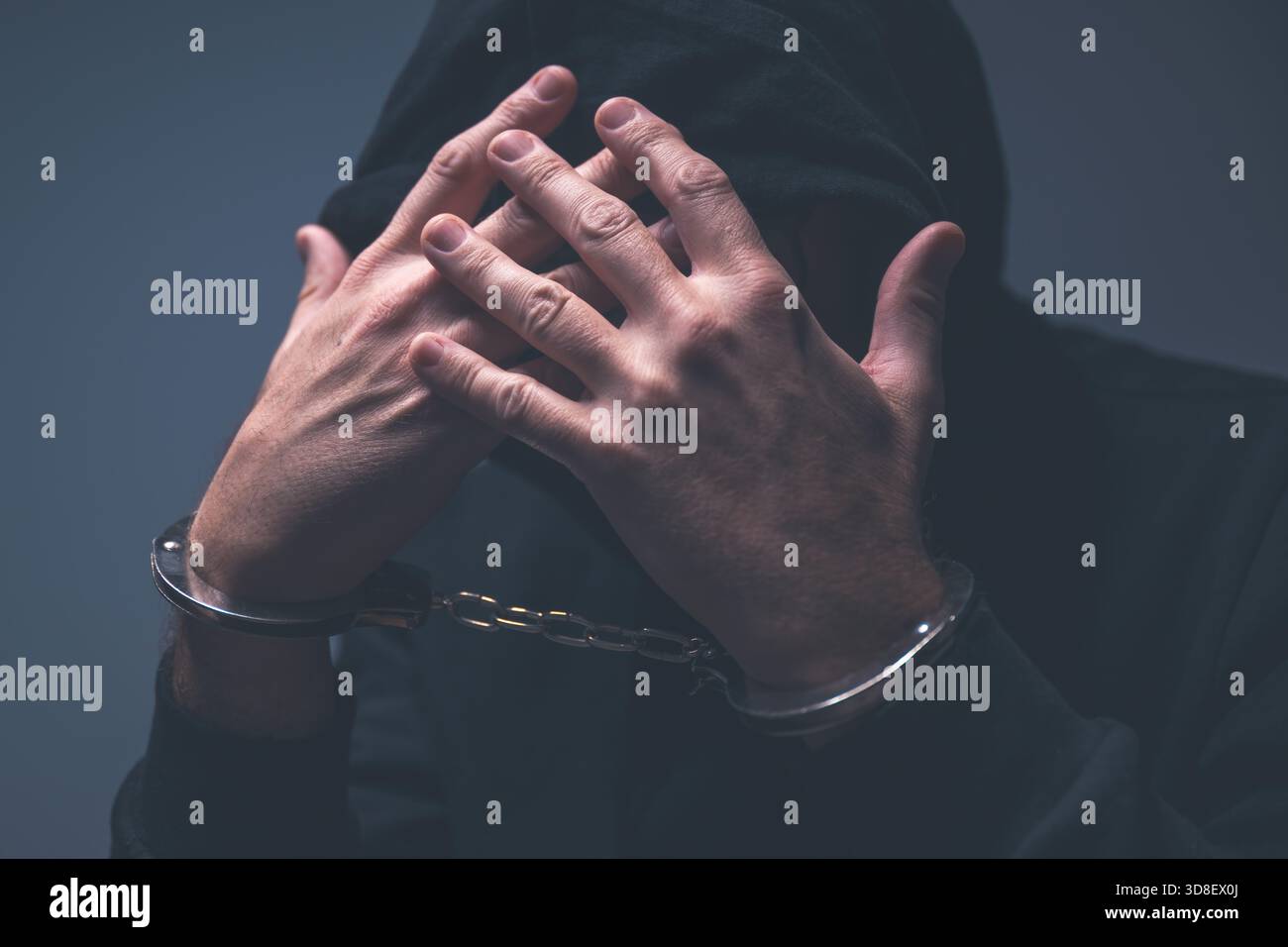 Low-key portrait of a hooded criminal with hands raised to an obscured ...