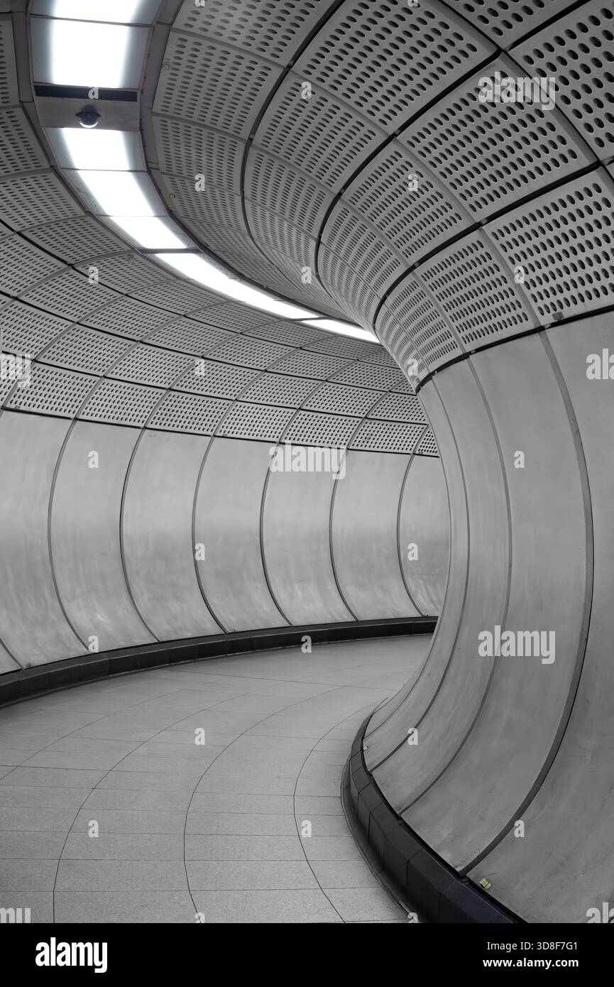 A modern, curved subway tunnel in London underground with smooth, gray ...