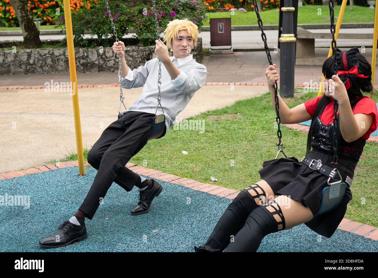 Two cosplayers are enjoying their time swinging on a swing set in a ...