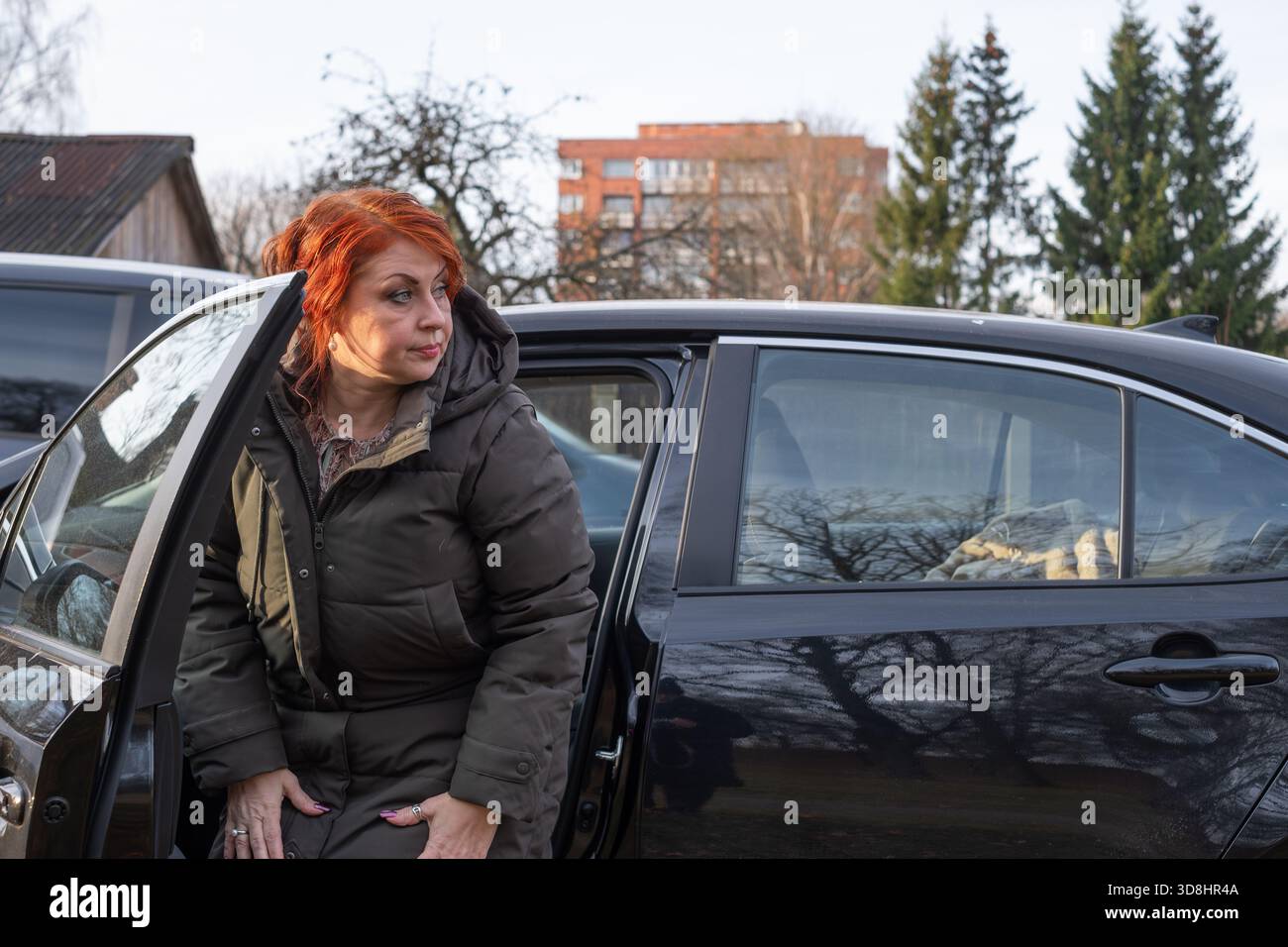 Female with red hair exits a black car, dressed in a cozy coat, with ...