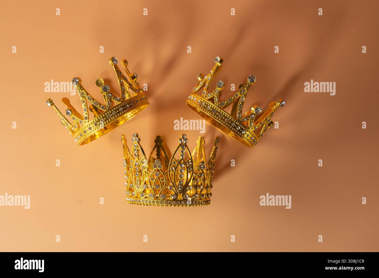 Three ornate golden crowns with sparkling jewels arranged on a warm ...