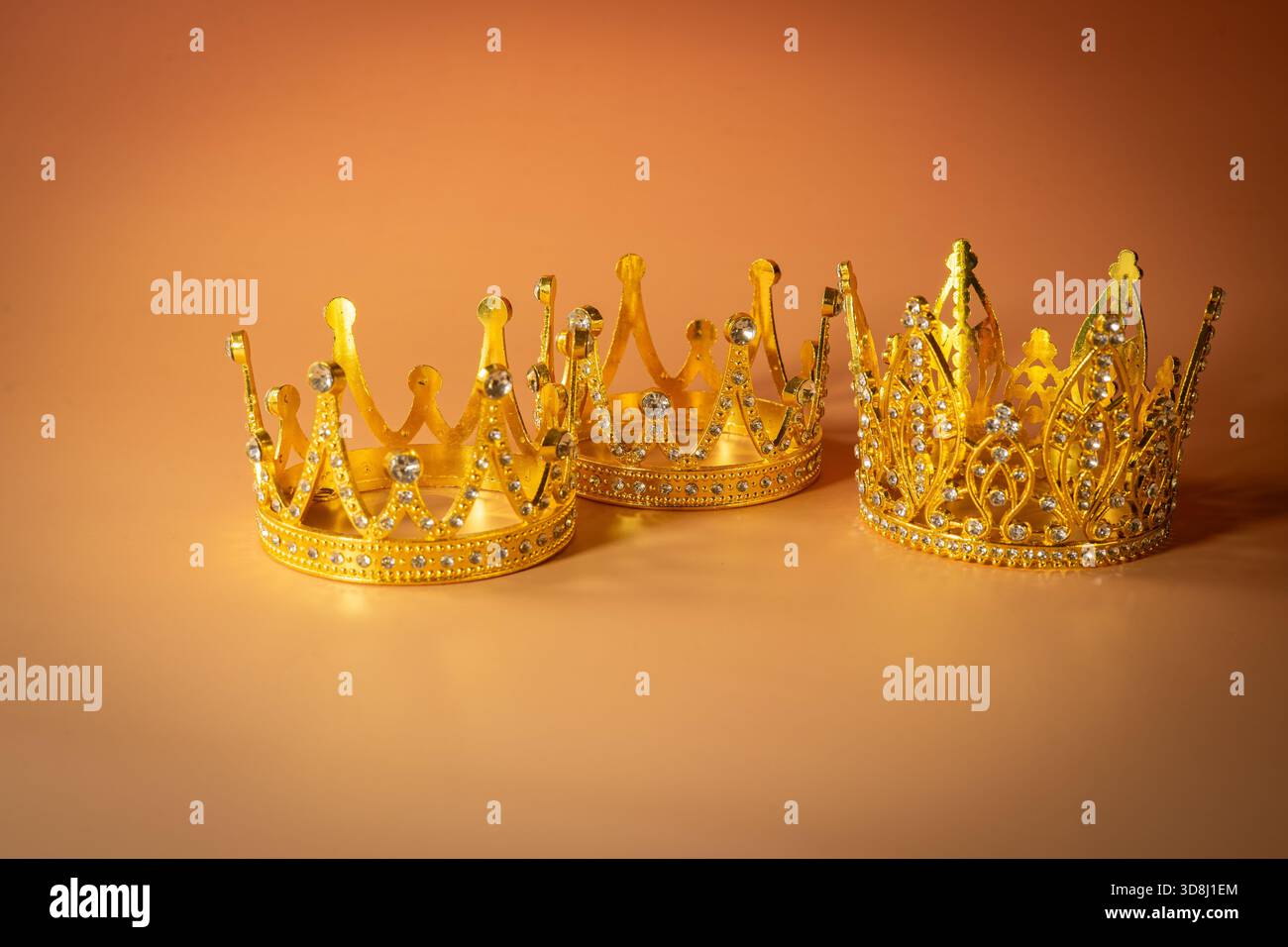 Three ornate golden crowns with sparkling jewels arranged on a warm ...