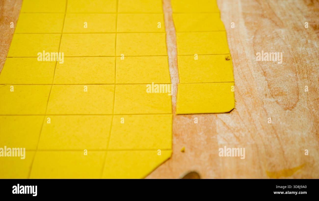 Fresh pasta dough is cut into small rectangular pieces on a flour ...