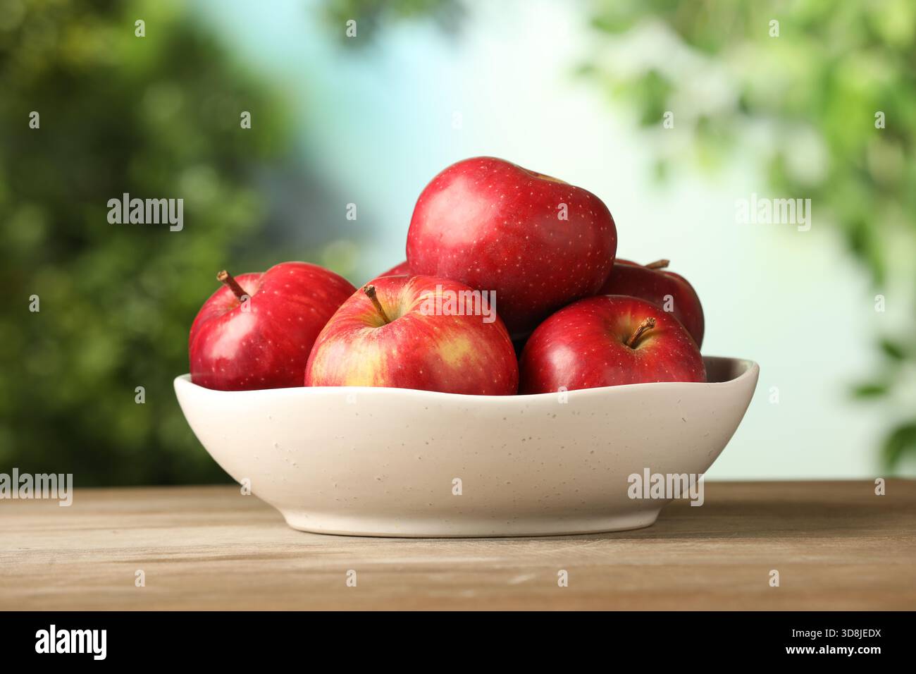 Ripe red apples in bowl on wooden table against blurred green ...