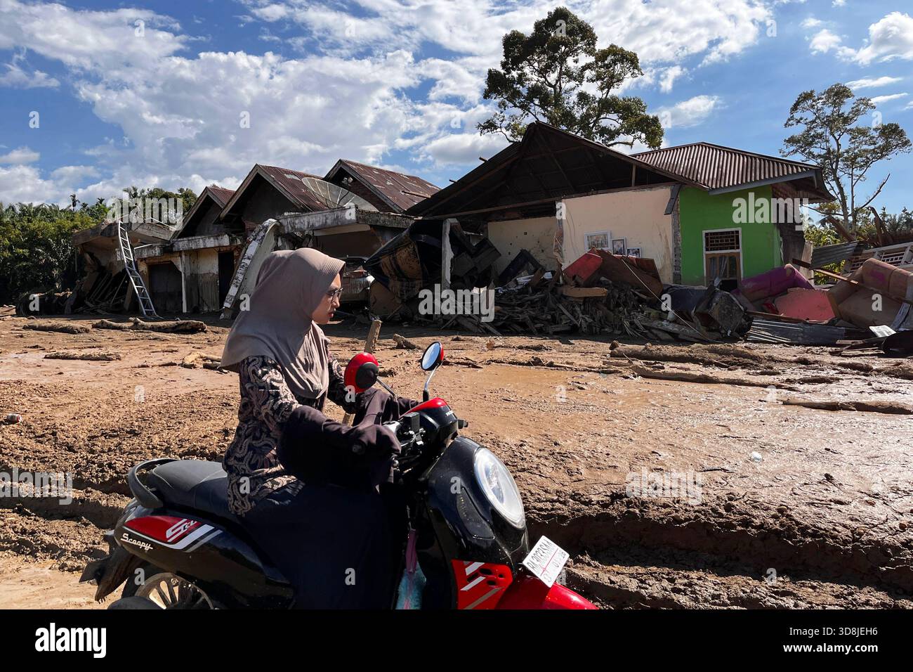 A motorist rides past houses damaged during a flash flood in Agam, West ...