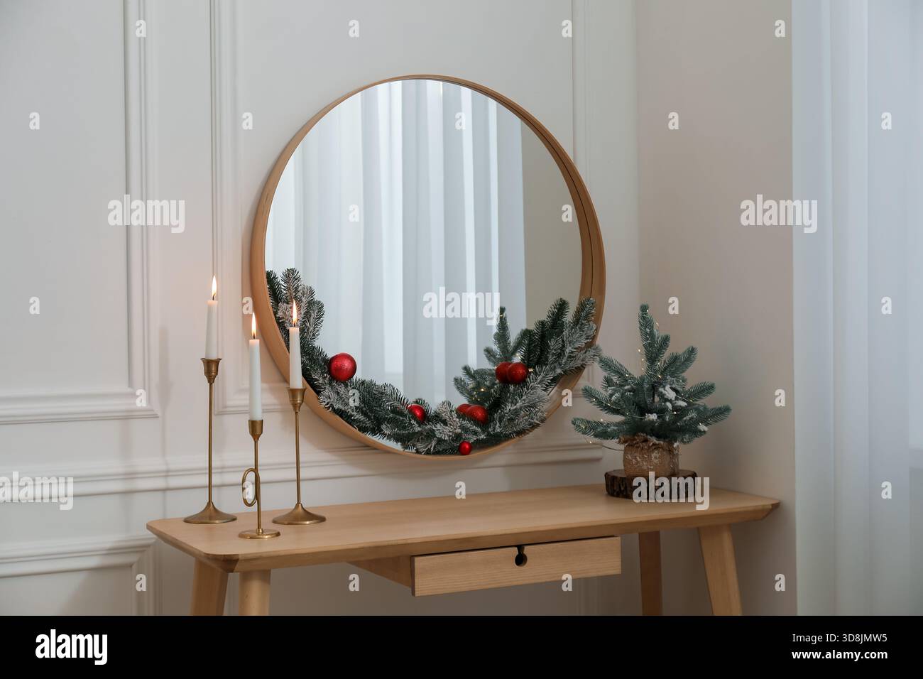 Mirror, burning candles and Christmas decor on console table near white ...