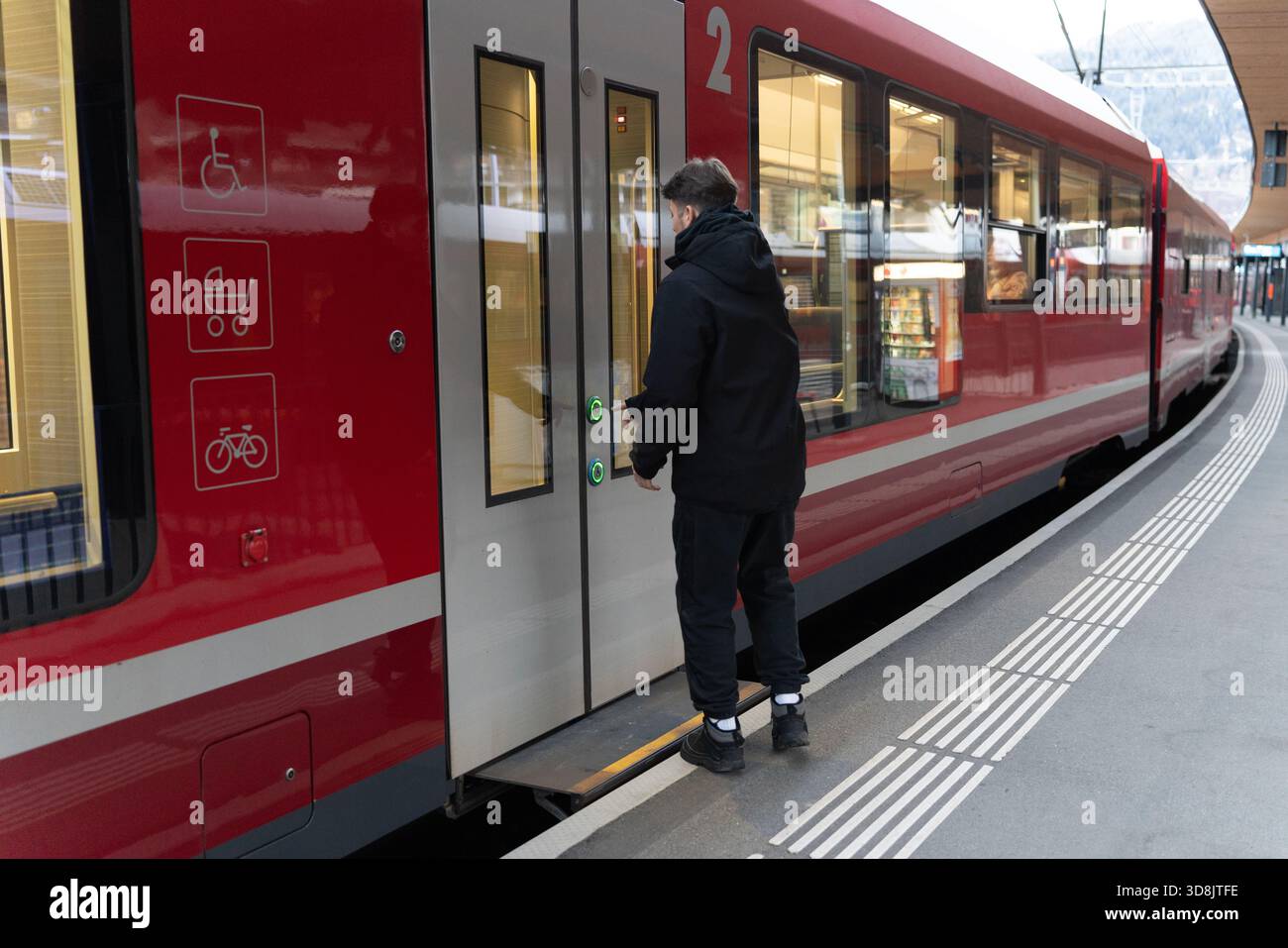 Passenger using a ramp to board a red train from a station platform ...