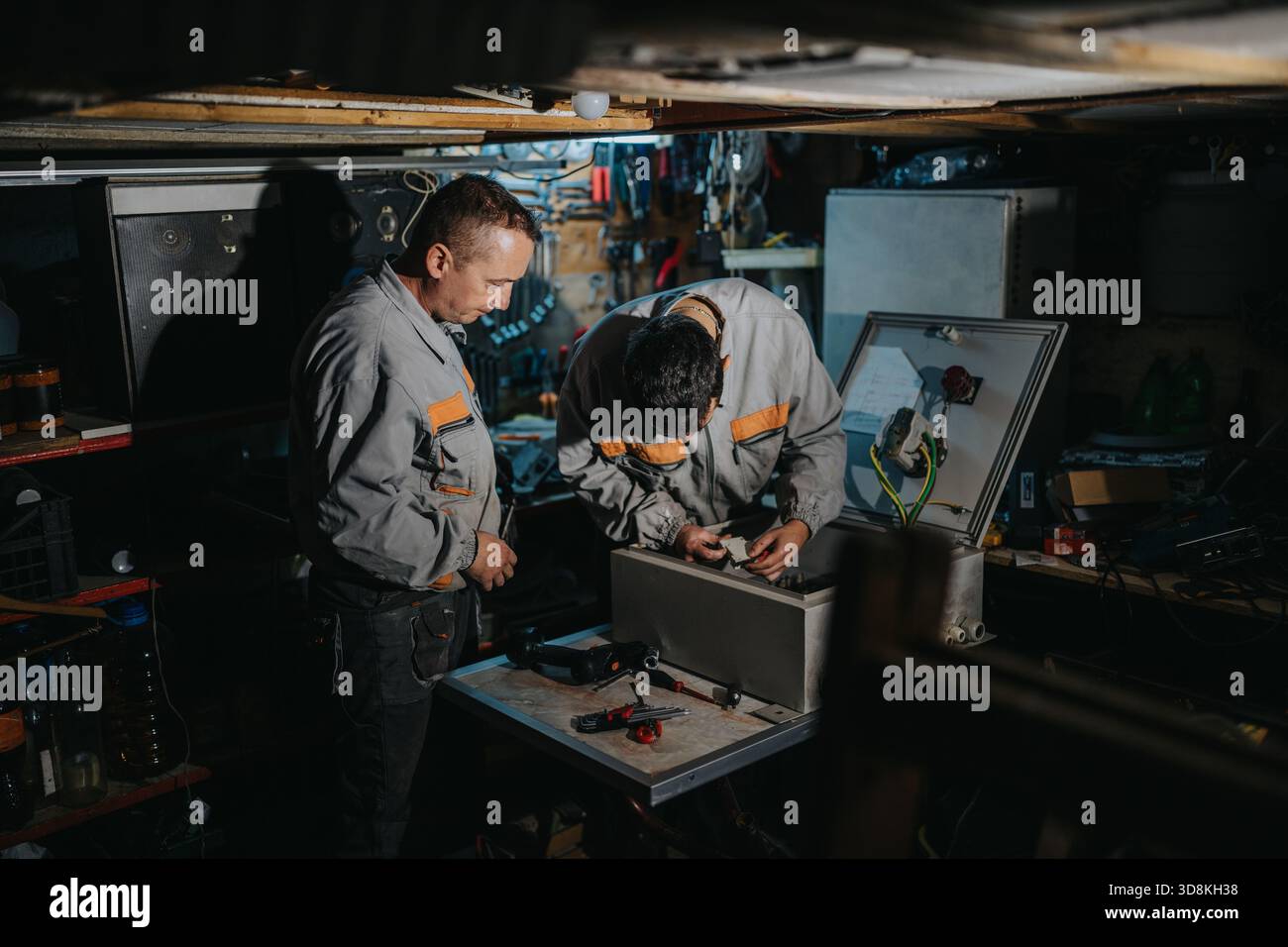 Two technicians working in a dim workshop repairing a metal device with ...