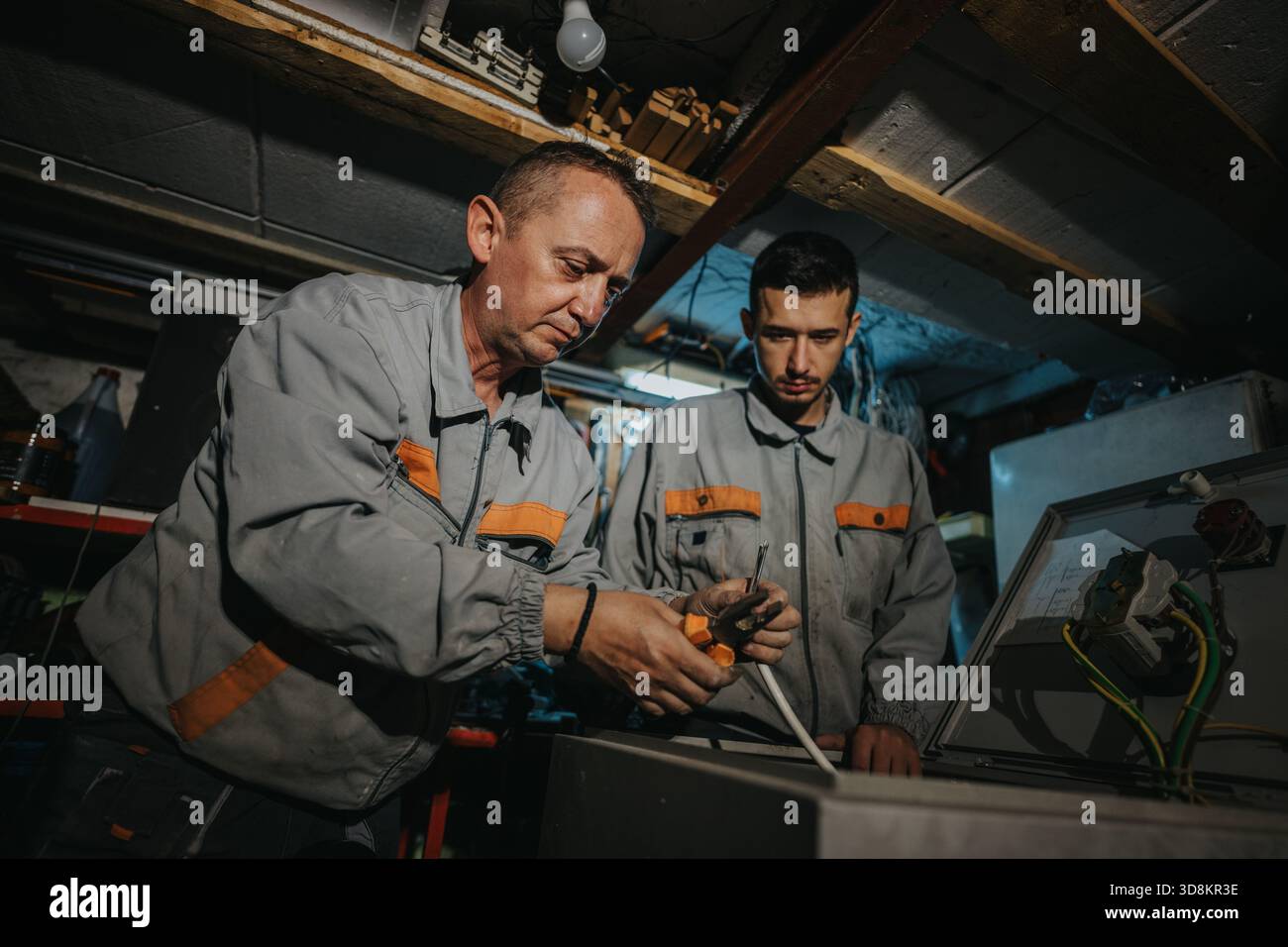 Two mechanics in gray uniforms work together on electrical equipment in ...
