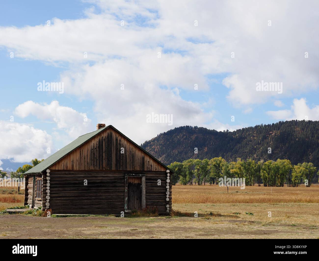 Rustic log pioneer cabin on wide prairie landscape with forested hill ...