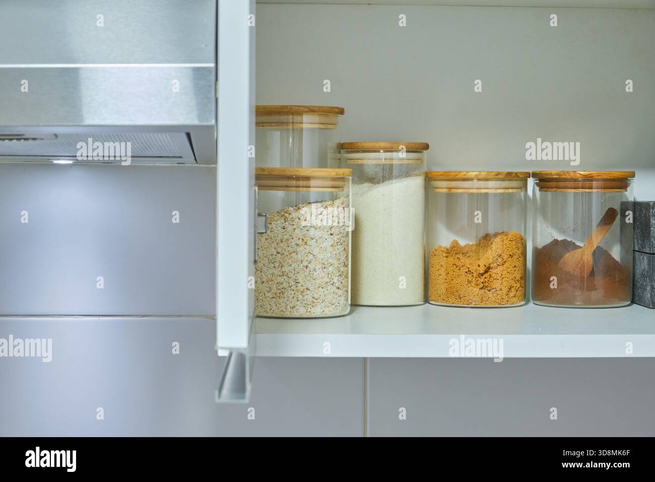Kitchen shelf storing oats, flour, cocoa, and brown sugar containers ...