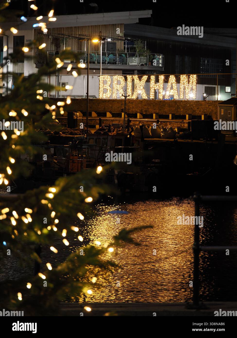 Illuminated BRIXHAM sign and festive tree lights reflected in harbour ...