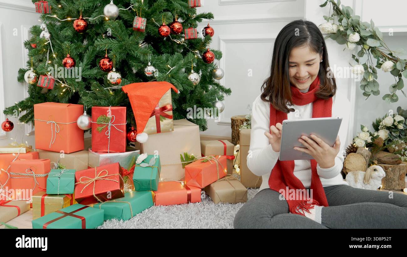 Asian woman using smart tablet sit at christmas tree xmas present gift ...