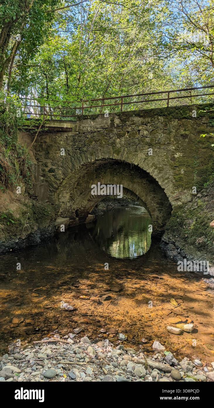 A charming old stone bridge crossing a small, clear stream in the heart ...