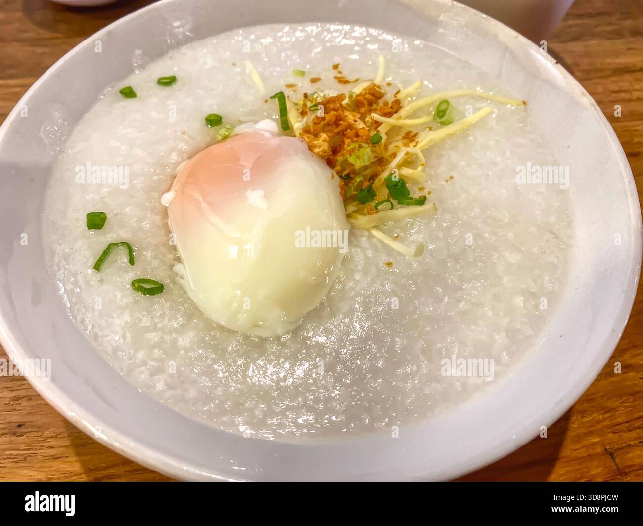 Bowl of hot rice porridge or congee topped with soft boiled egg, ginger ...