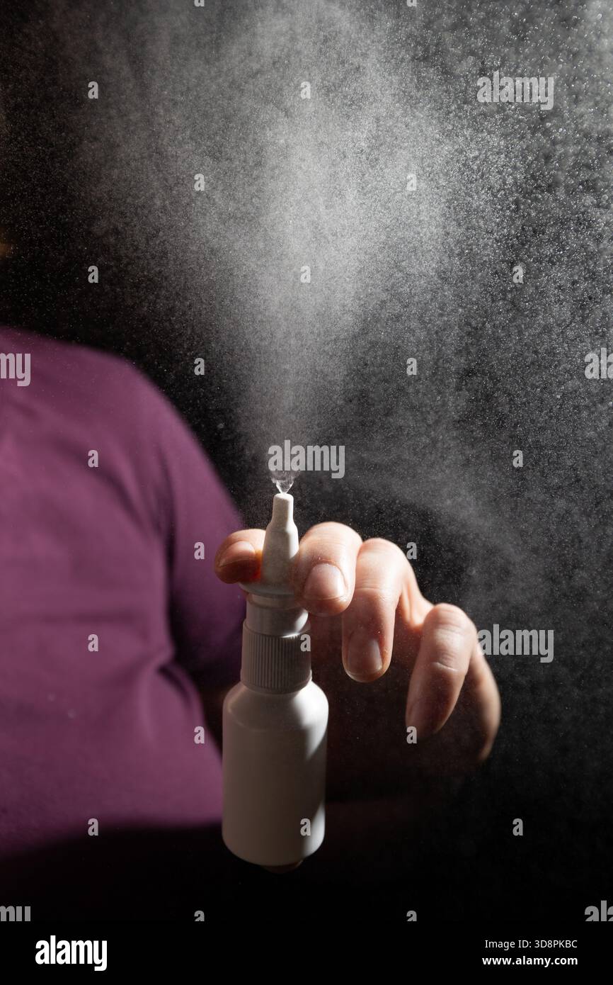 A person is using a nasal spray, showcasing the release of mist. This ...