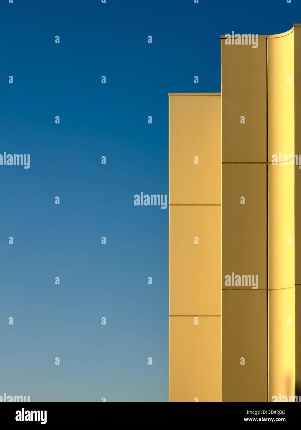 Sunlight casts warm hues and sharp shadows on a contemporary building's ...