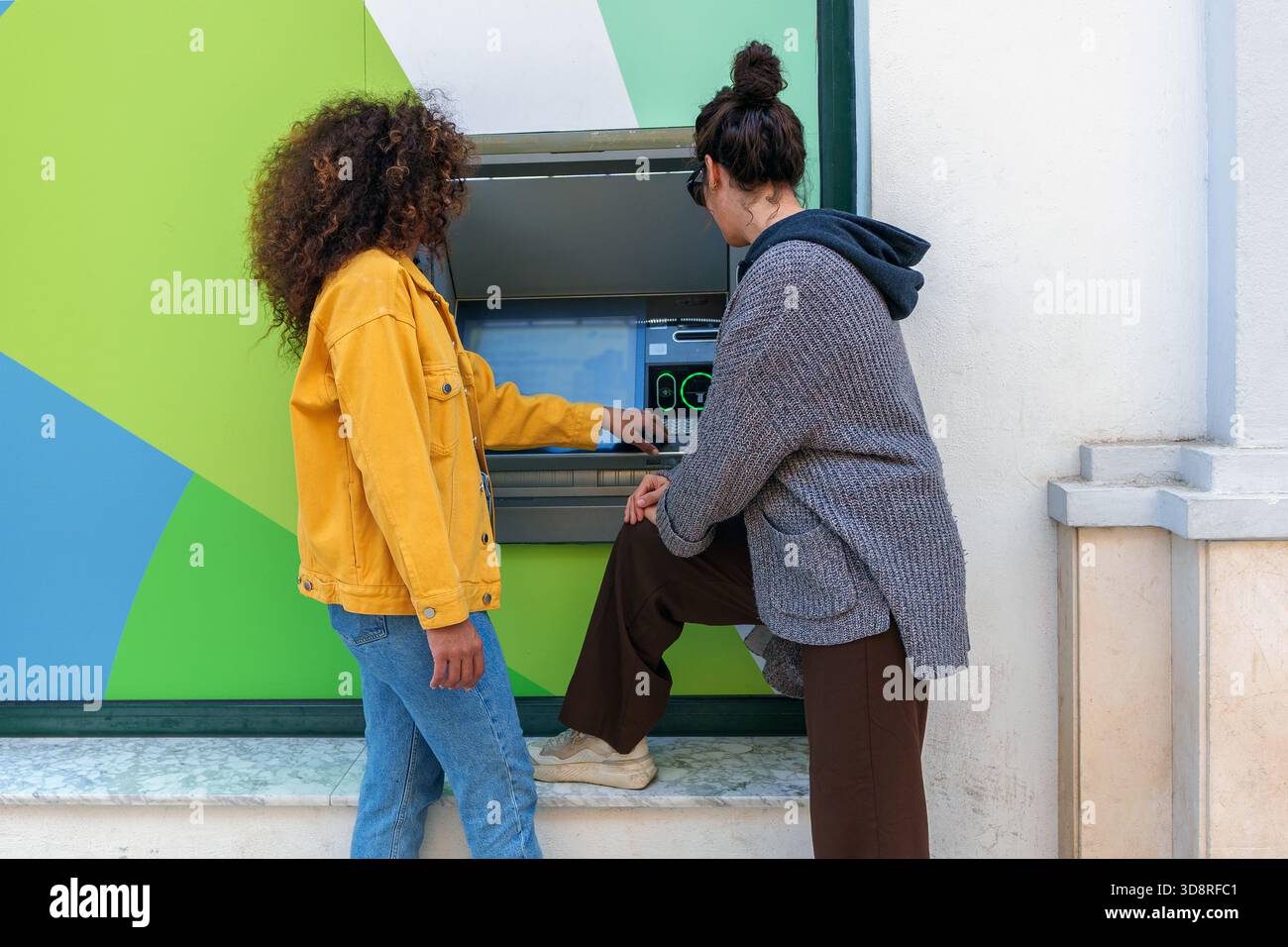 Two young women performing a digital banking operation at an ATM on a ...