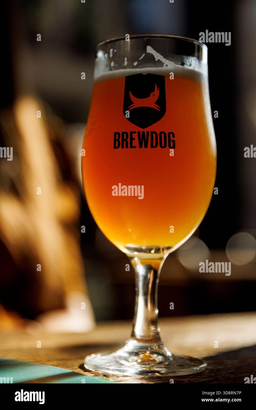 A glass of amber craft beer stands on a wooden table with blurred ...