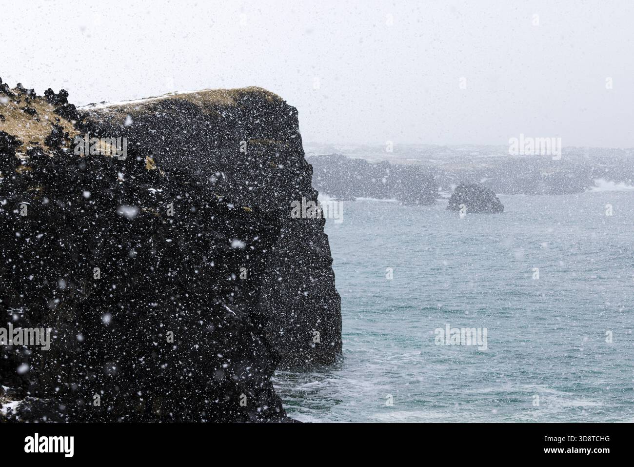 View of a dramatic black lava cliff face meeting the turbulent, teal ...