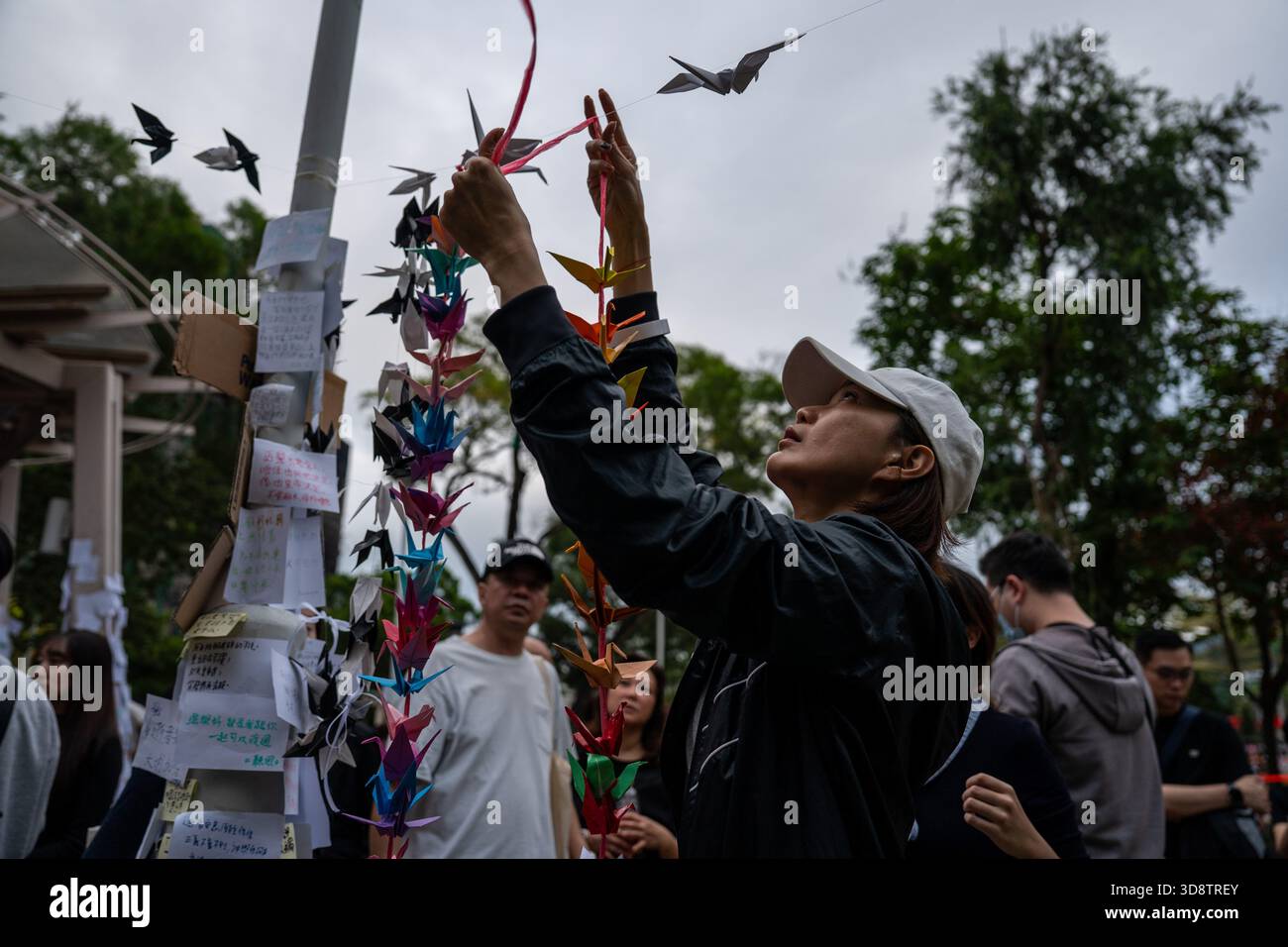 A mourner placing origami crane on a string at a makeshift memorial ...