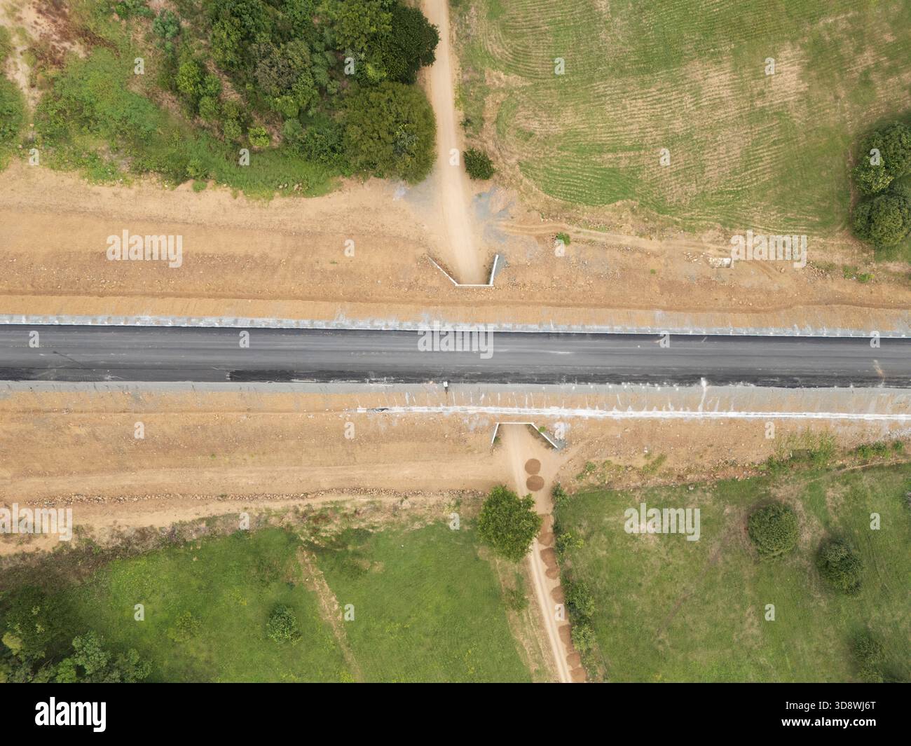 A view of a freshly paved road crossing through fields and trees in a ...