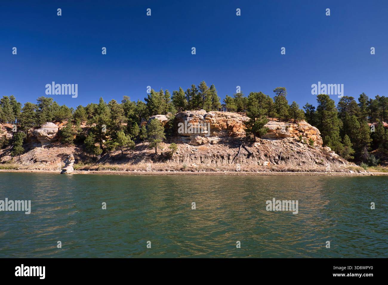 Rock formation and pine trees next to the water on a summer day at ...