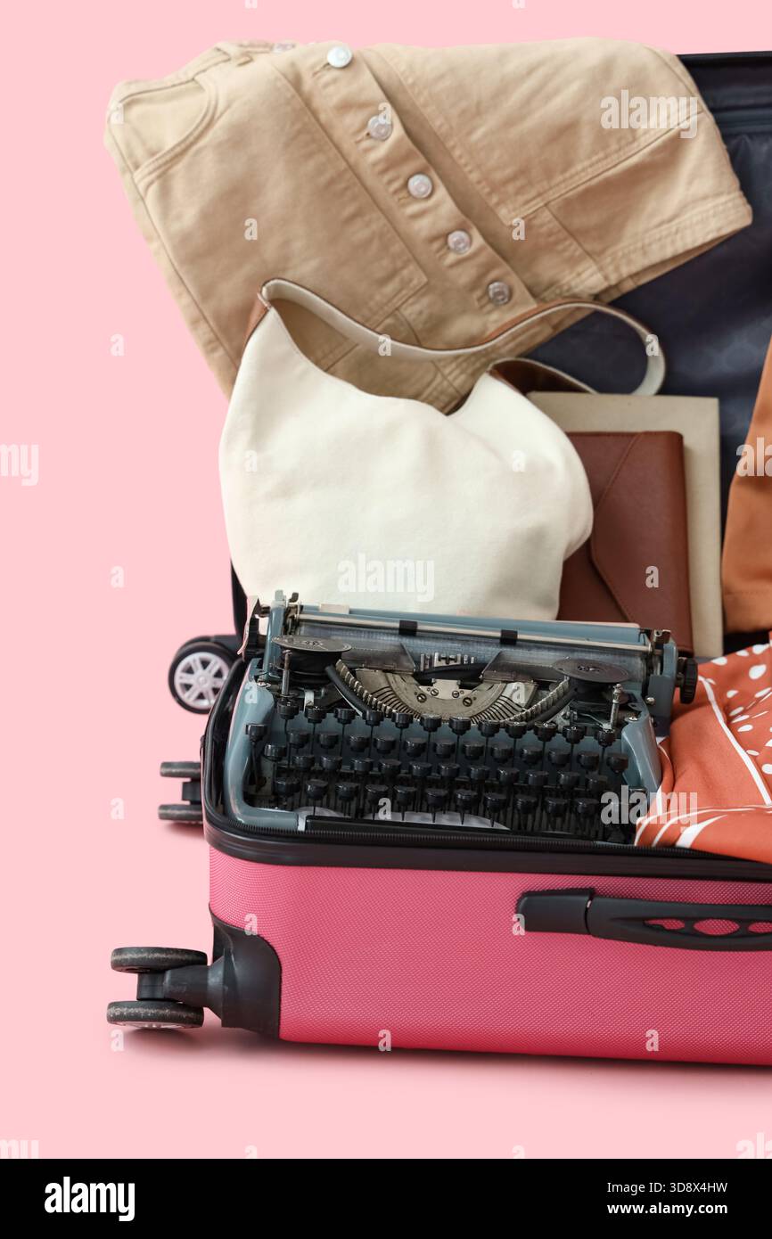 Open suitcase with vintage typewriter and female clothes on pink ...