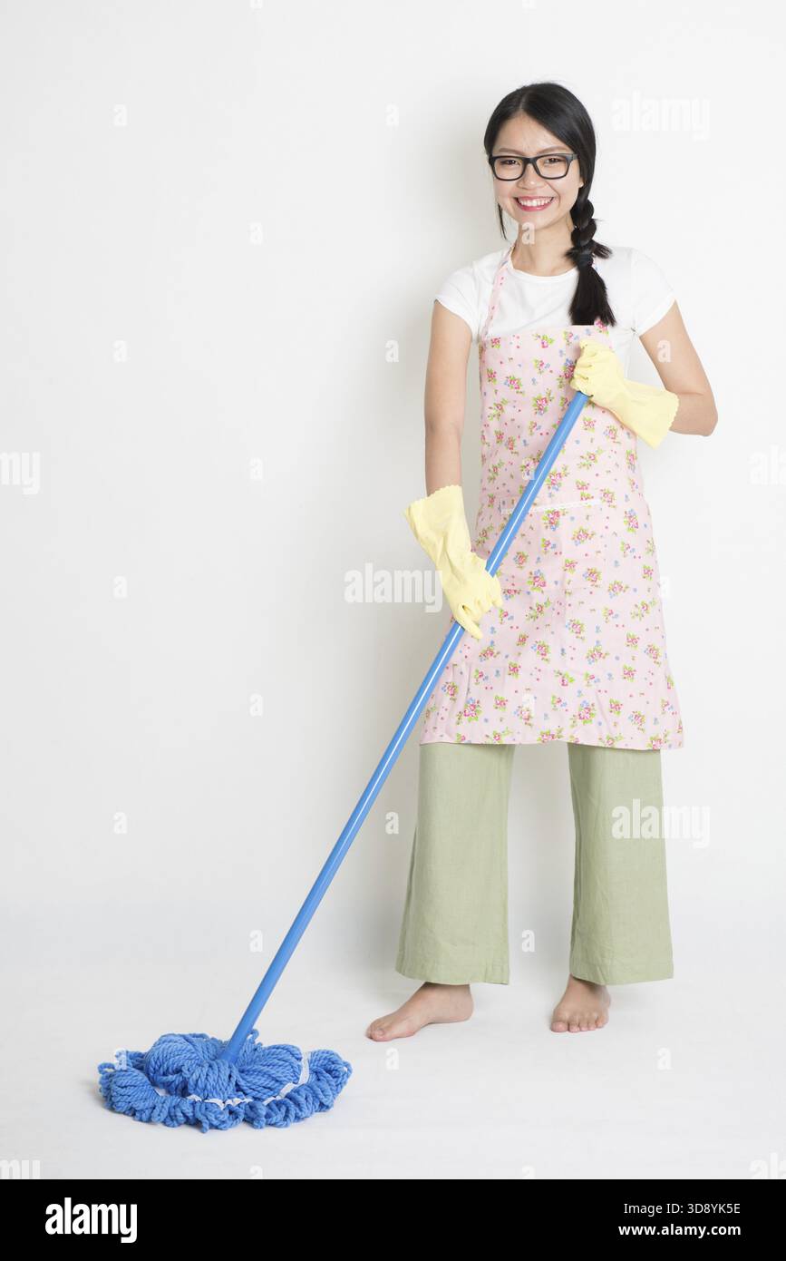 Full length Asian Chinese girl housekeeping, mopping floor on plain ...