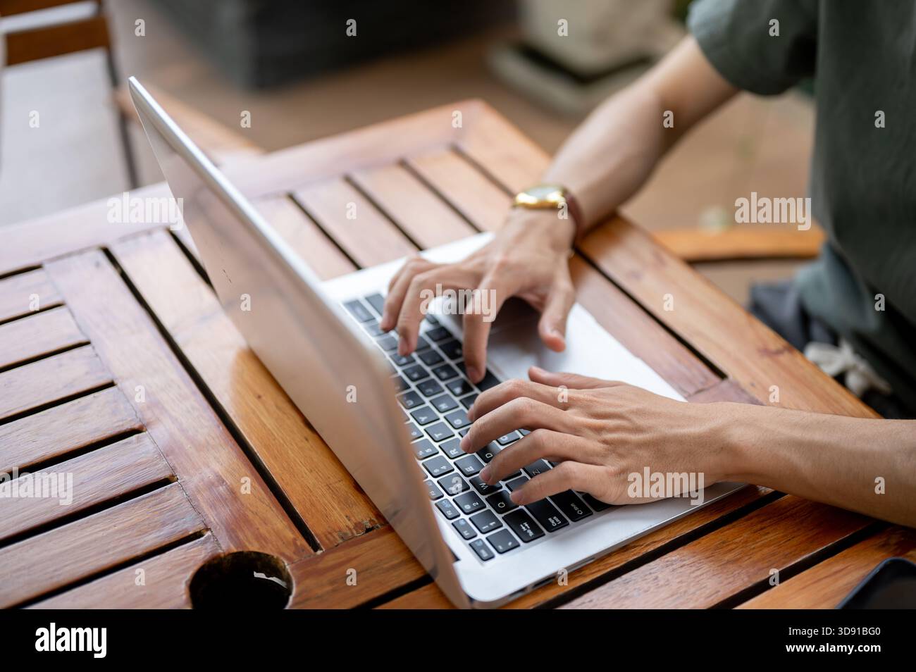 Close up of a pair of man hands wearing a watch typing on his laptop ...
