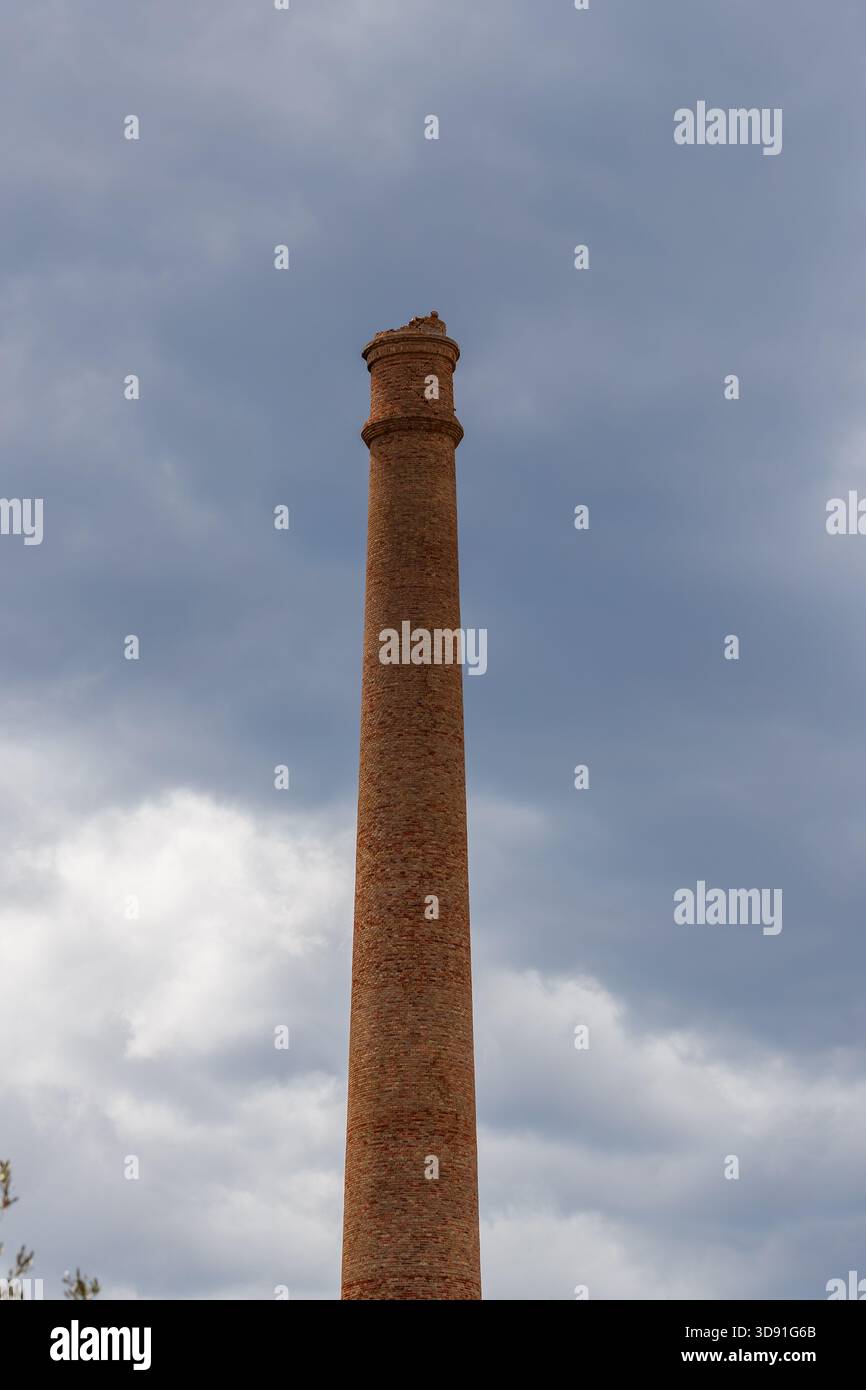 A tall, slender brick industrial chimney stands weathered and silent ...