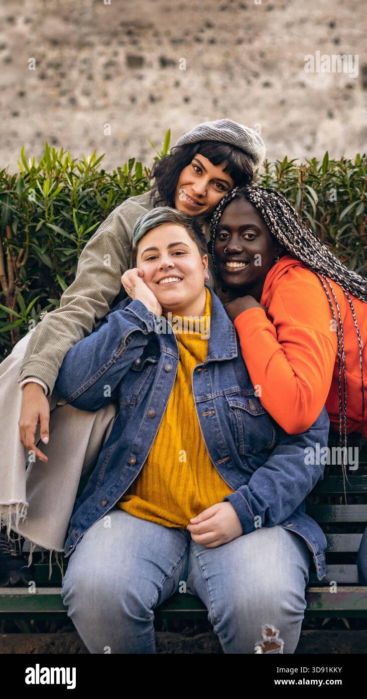 Vertical shot of three diverse young friends smiling and hugging while ...