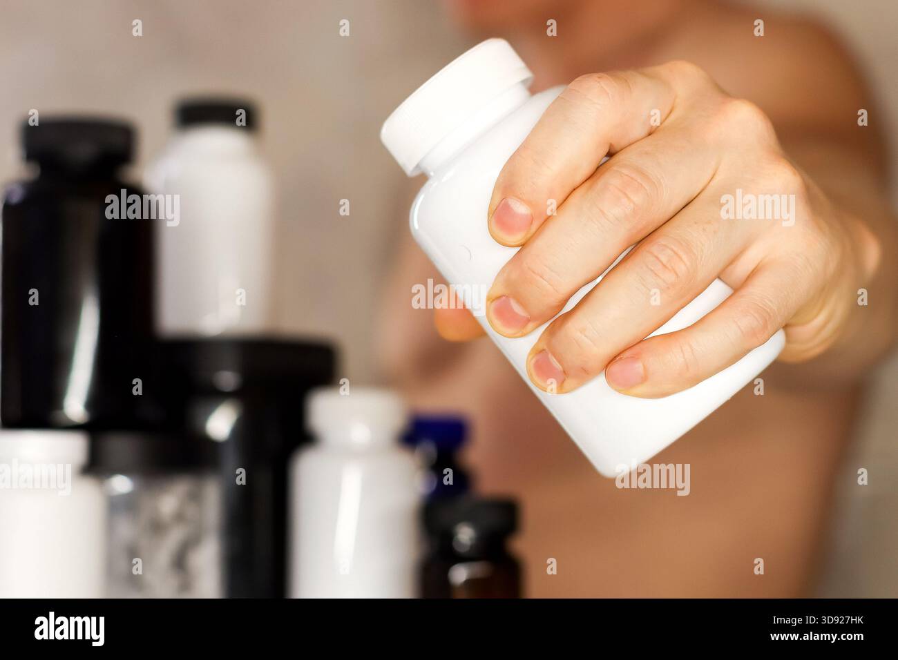 Hand tilting white supplement bottle to pour contents amid blurred jars ...