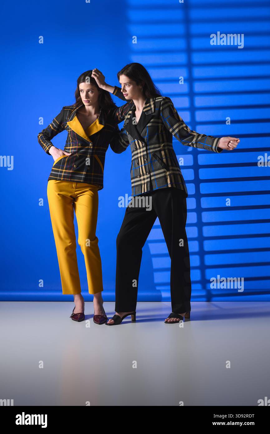 Two young beautiful twin sisters model chic attire while striking ...