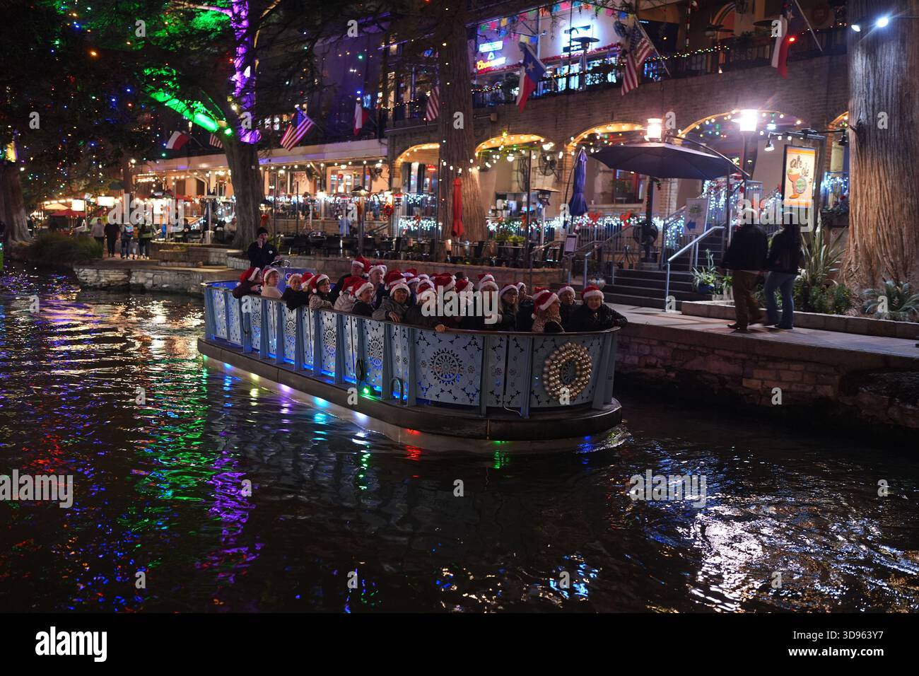 A group in Santa hats ride a barge as they view holiday lights along ...