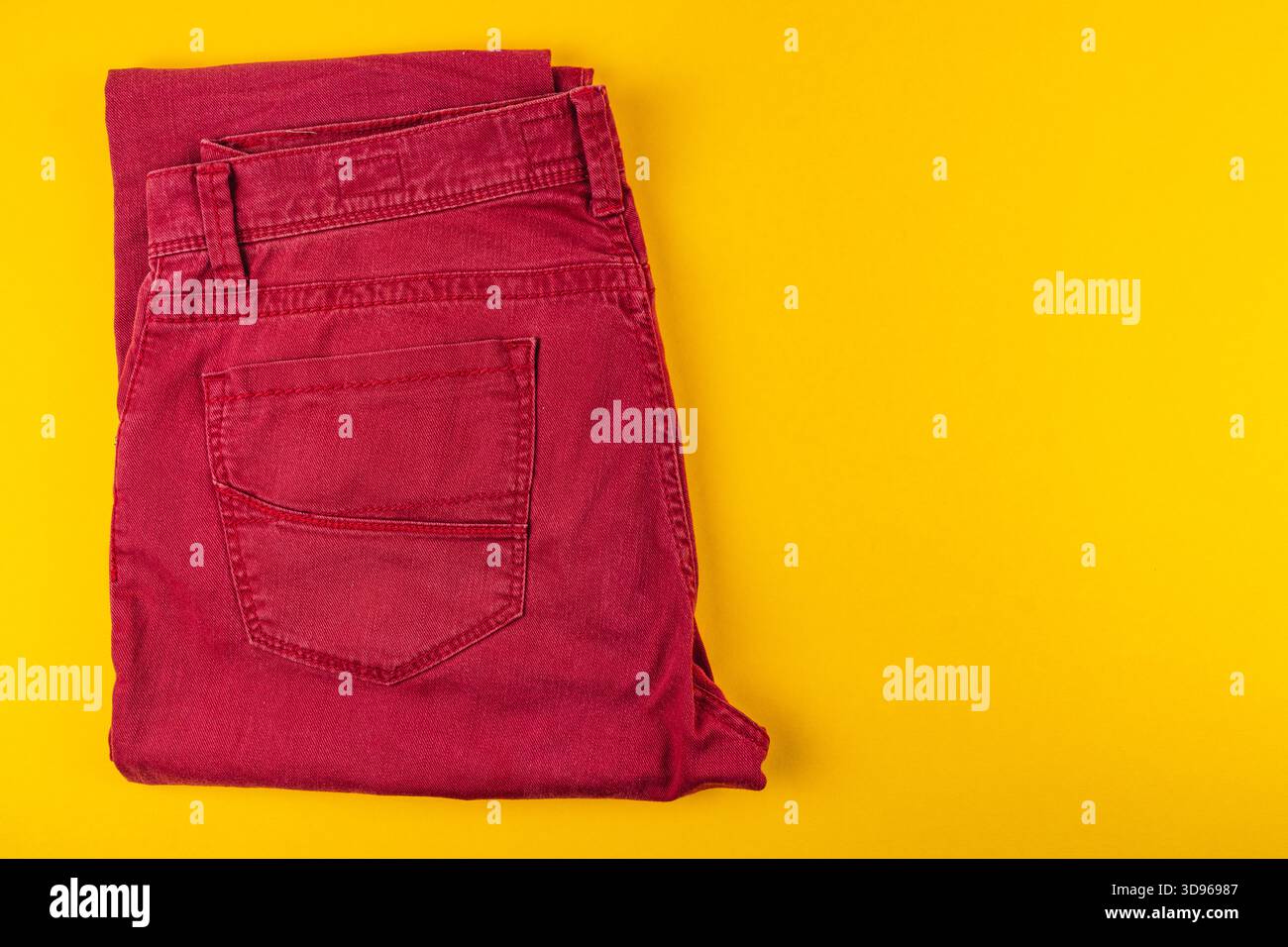 Folded red jeans sit neatly against a vibrant yellow background ...