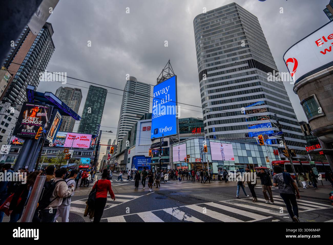 Crowds cross a wet street under large digital billboards and modern ...