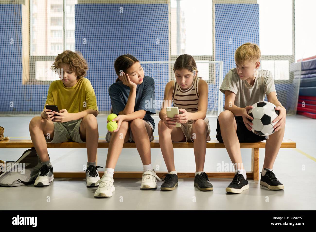 Group of four teenagers sitting on bench using smartphones and holding ...