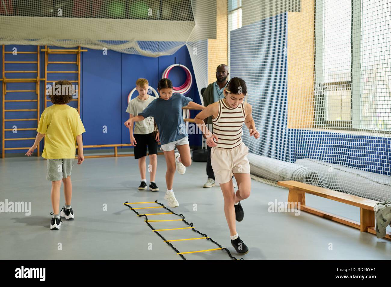 Group of multiethnic children exercising in gym, jumping over agility ...