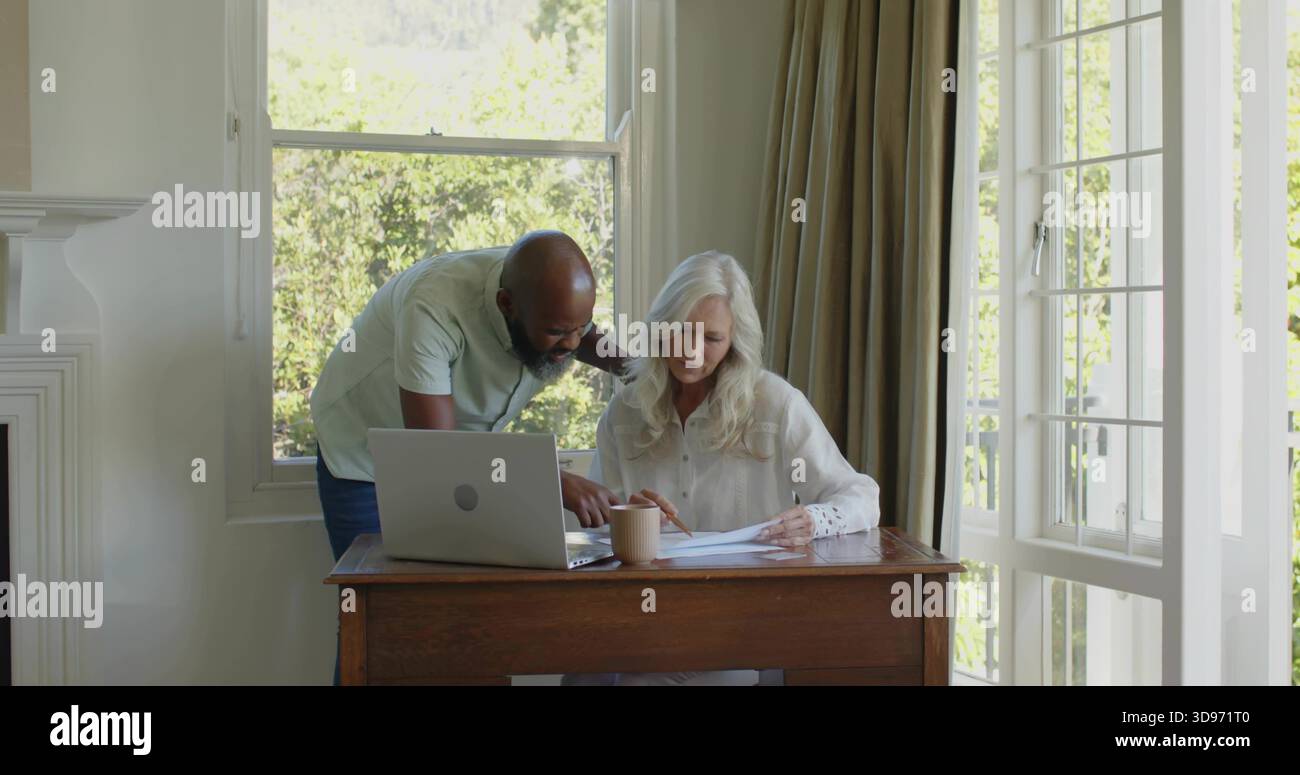 Reviewing couple leaning over wooden desk at home, pointing at ...