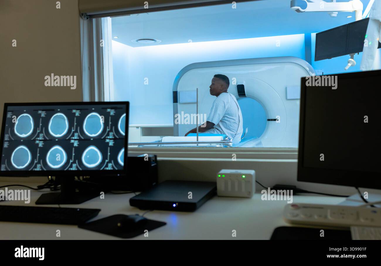 African American man in gown sitting on MRI table in control room ...