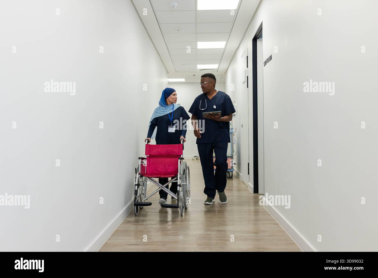 African American coworkers walking ward pushing red wheelchair holding ...