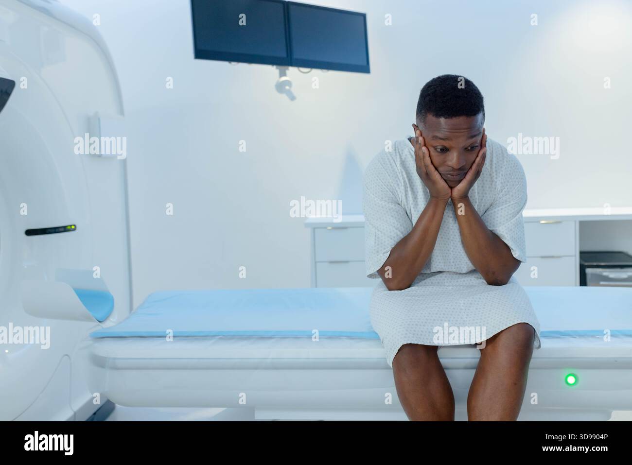 African American man wearing gown sitting on scanner bed in imaging ...