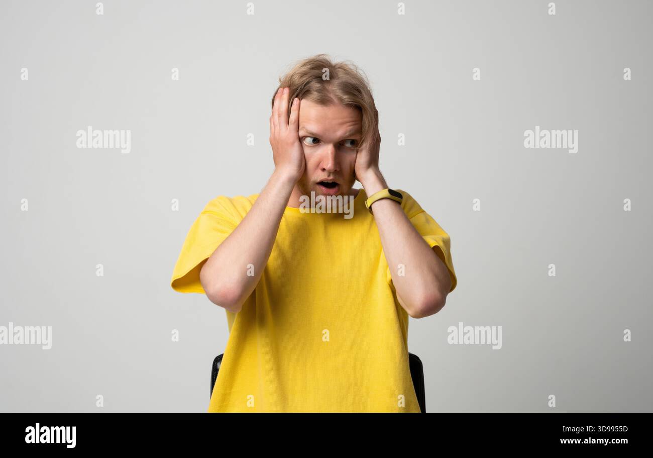 Shocked young man holding his cheeks with both hands and reacting with ...